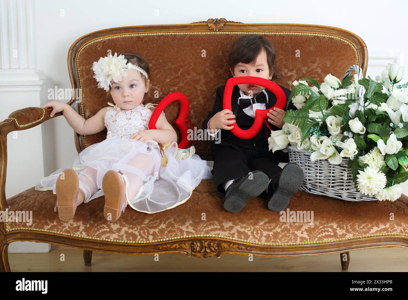 Beautiful little kids in costumes bride and groom sitting on couch with ...