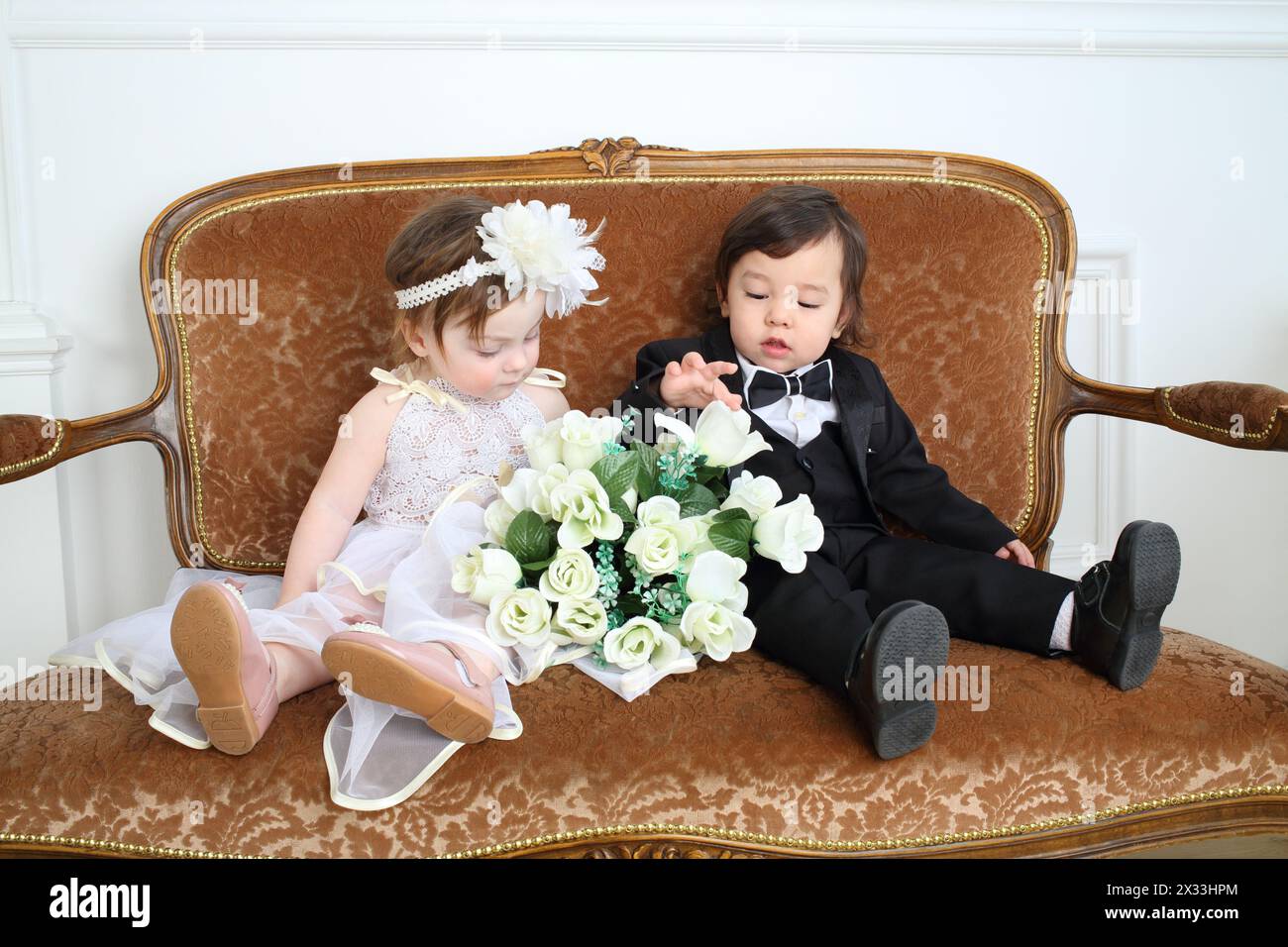 Beautiful little kids in costumes bride and groom sitting on couch with ...