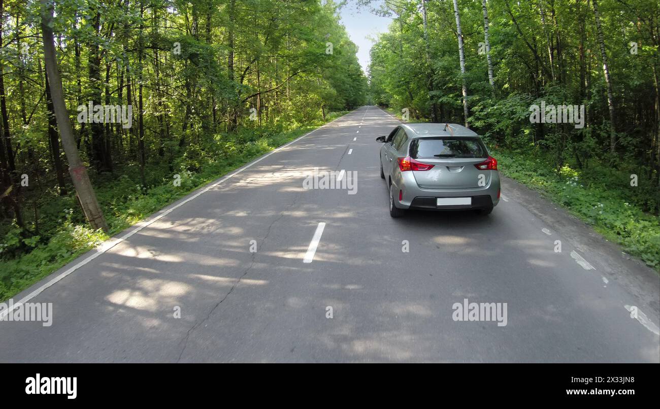 Car drives by road among trees with green foliage at summer day in ...