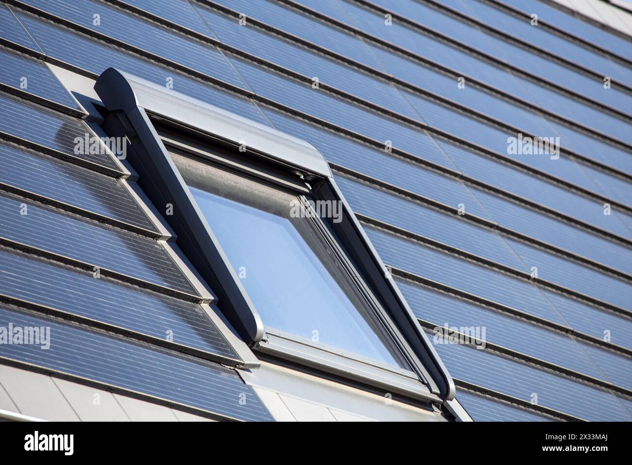 Roof window on a detached house with solar roof tiles. Solar tiles are ...