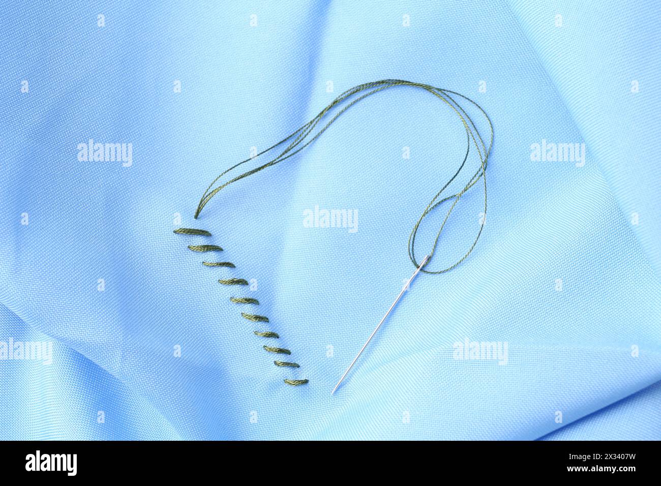 Sewing needle with thread and stitches on light blue cloth, top view ...