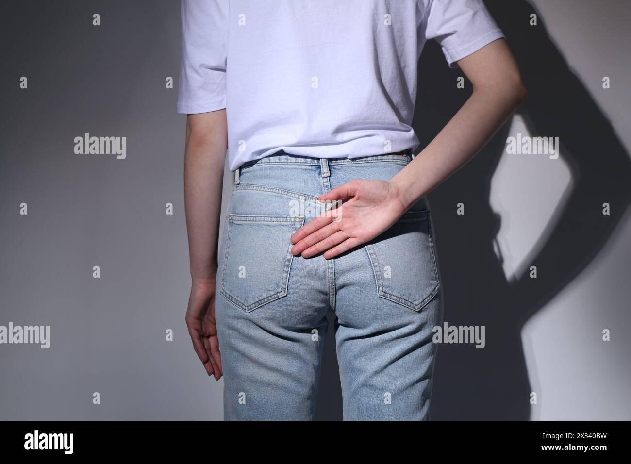 Woman showing open palm behind her back on grey background, back view ...