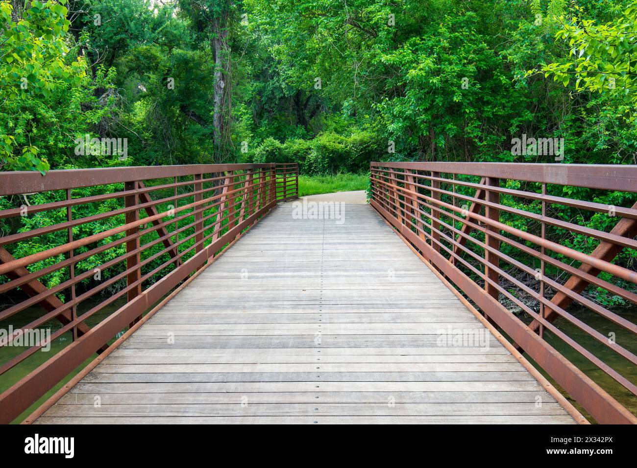 A rustic wooden bridge, adorned with rust-colored railings, beckons ...