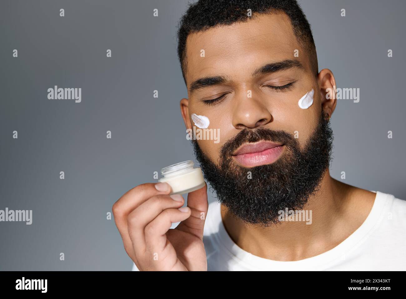 A handsome young man with a beard applying cream to his face Stock ...