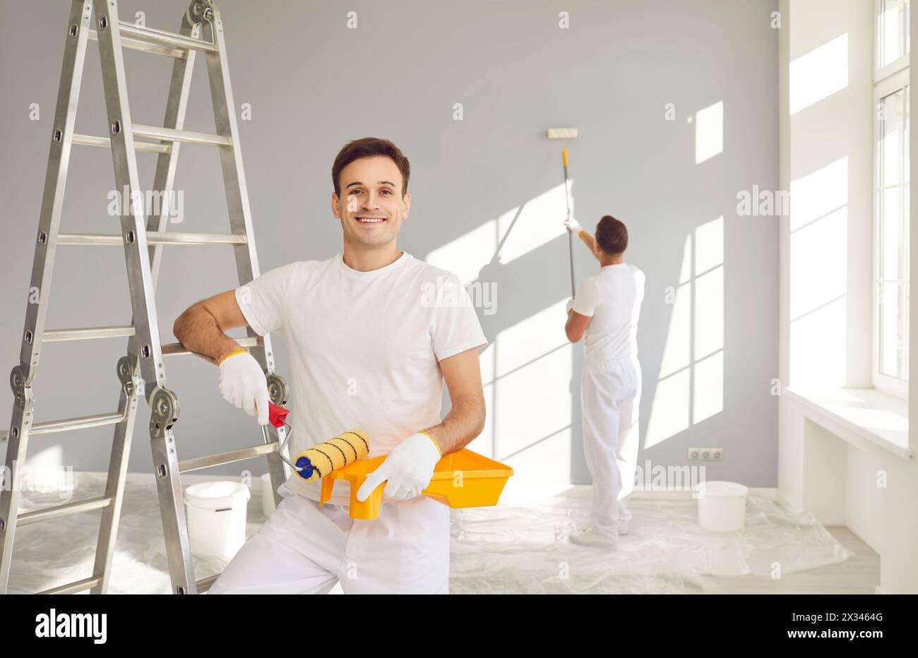 Portrait of happy male wall painter with paint roller and tray standing ...