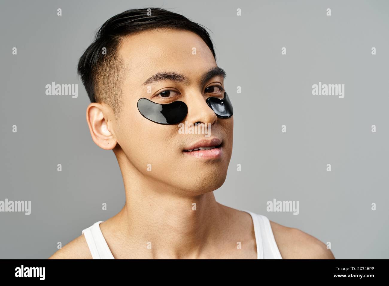 Handsome Asian man in a grey studio using eye patches for his beauty ...