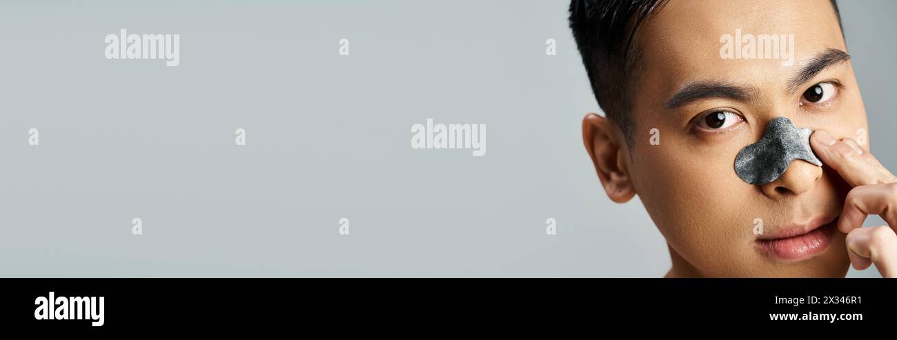 A portrait of a handsome Asian man with a beauty nose patch in a grey ...