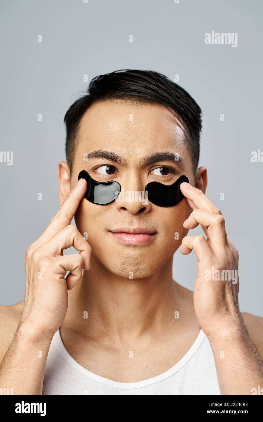 Handsome Asian man holding two black circles over his eyes in a beauty ...