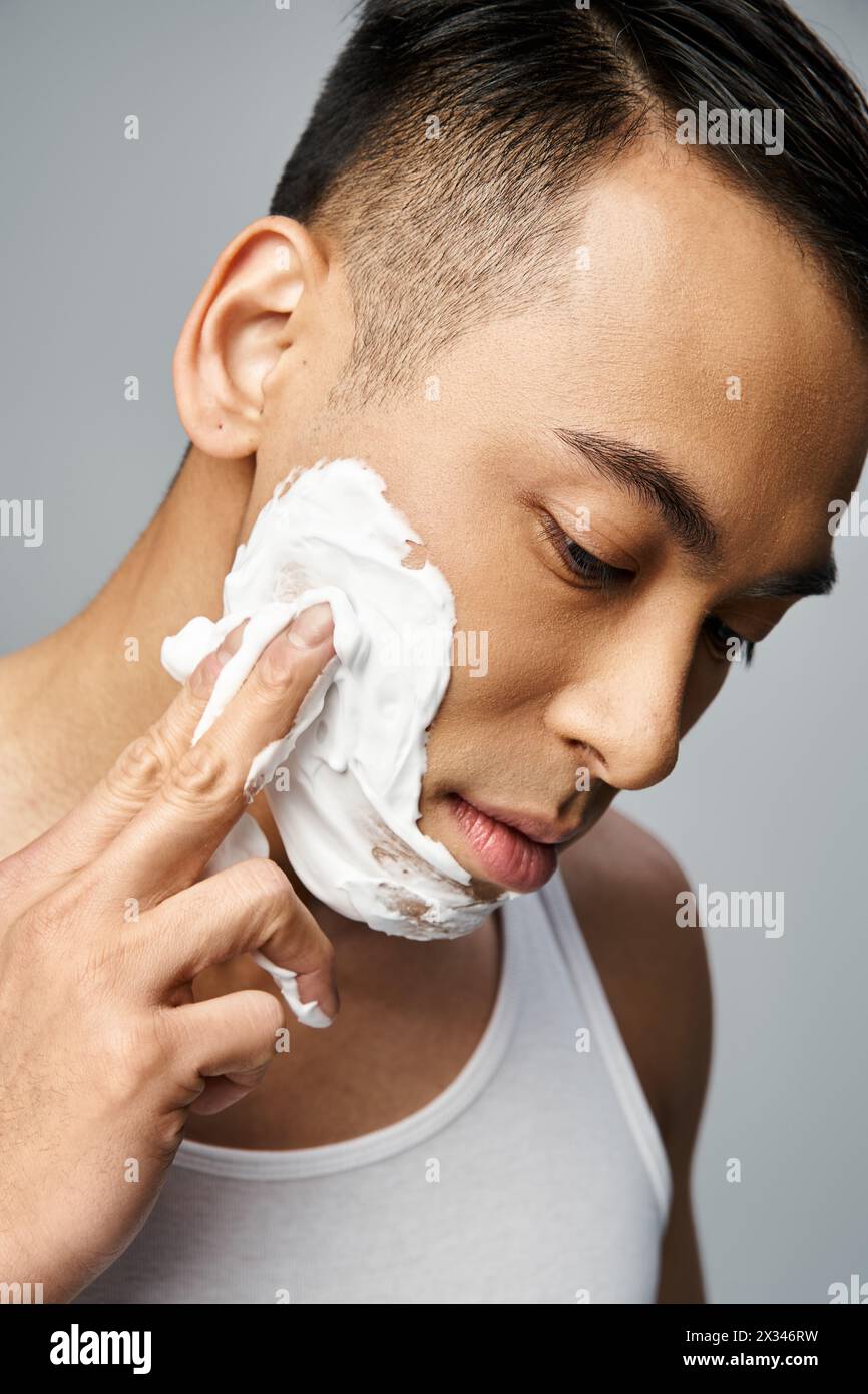 A handsome Asian man applying shaving foam on his face in a grey studio setting Stock Photo - Alamy