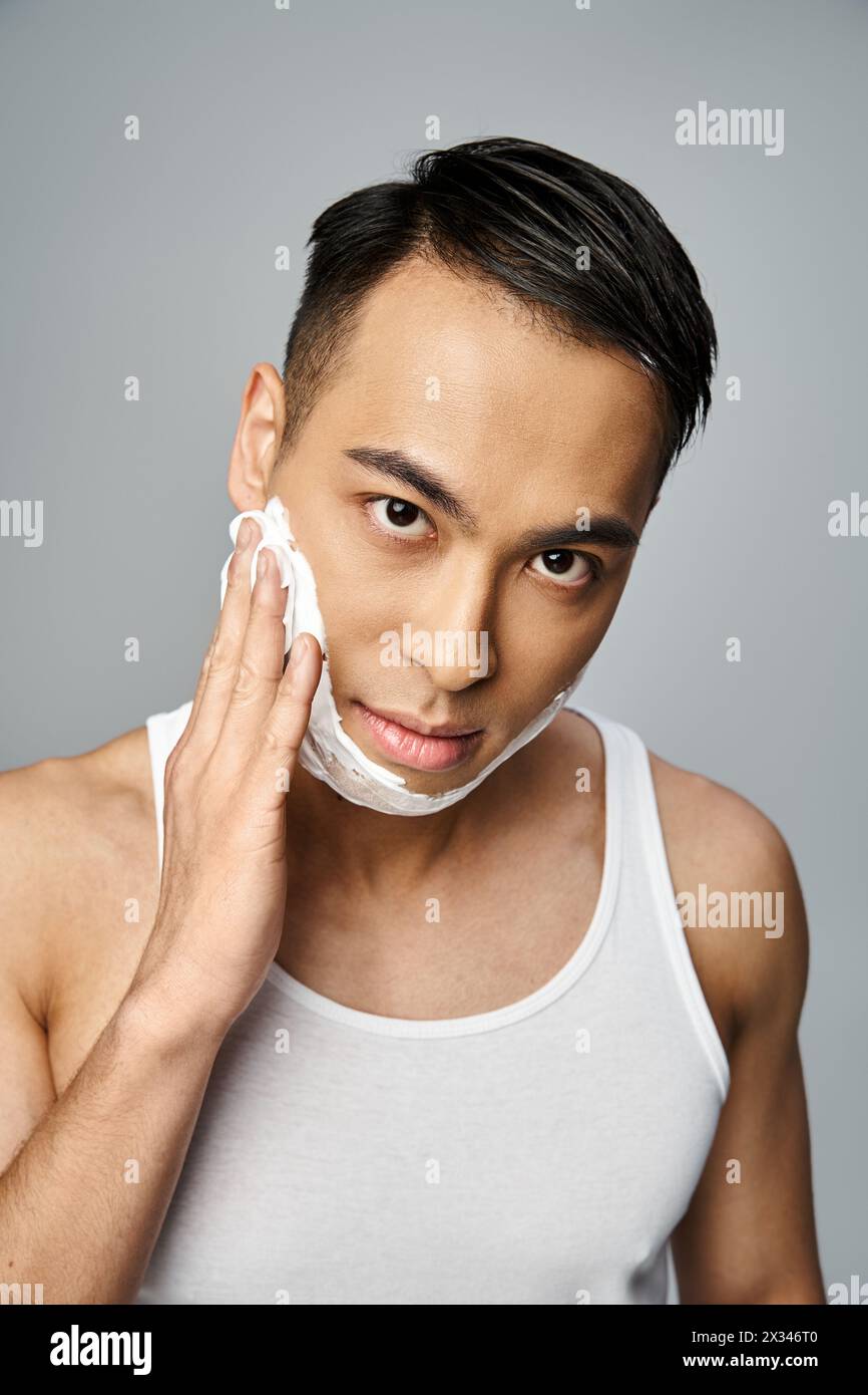 Handsome Asian man with shaving foam on face, gracefully shaving in a grey studio Stock Photo ...