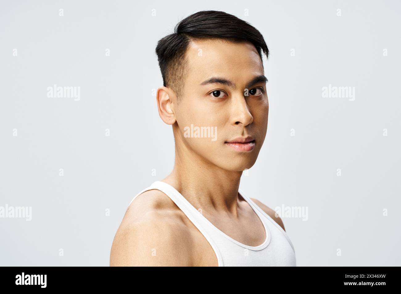 A handsome Asian man in a tank top strikes a confident pose in a grey ...