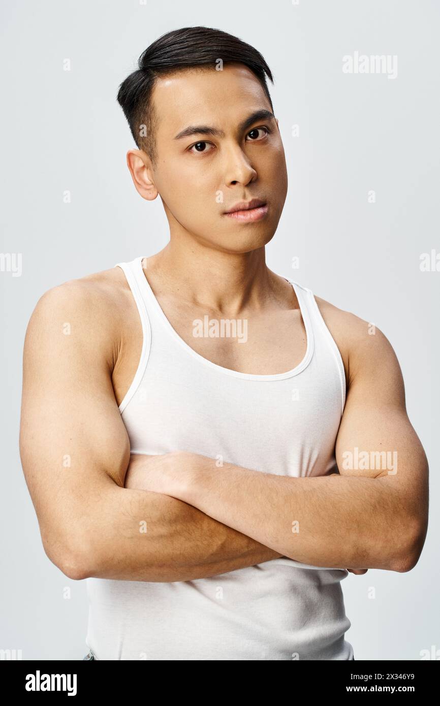 A handsome Asian man confidently poses with his arms crossed in a grey ...