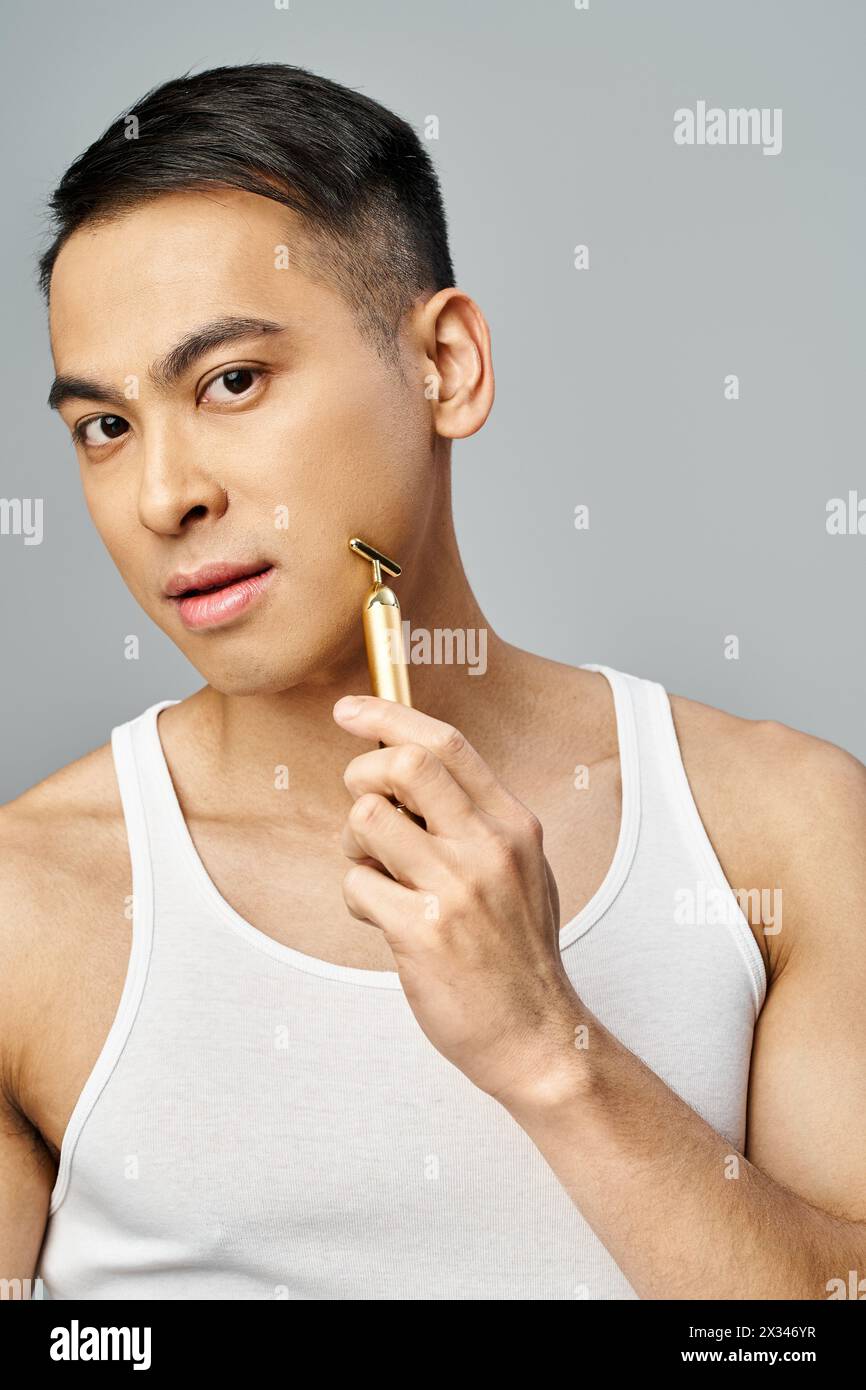 Asian man with a stylish appearance shaving in a grey studio setting ...