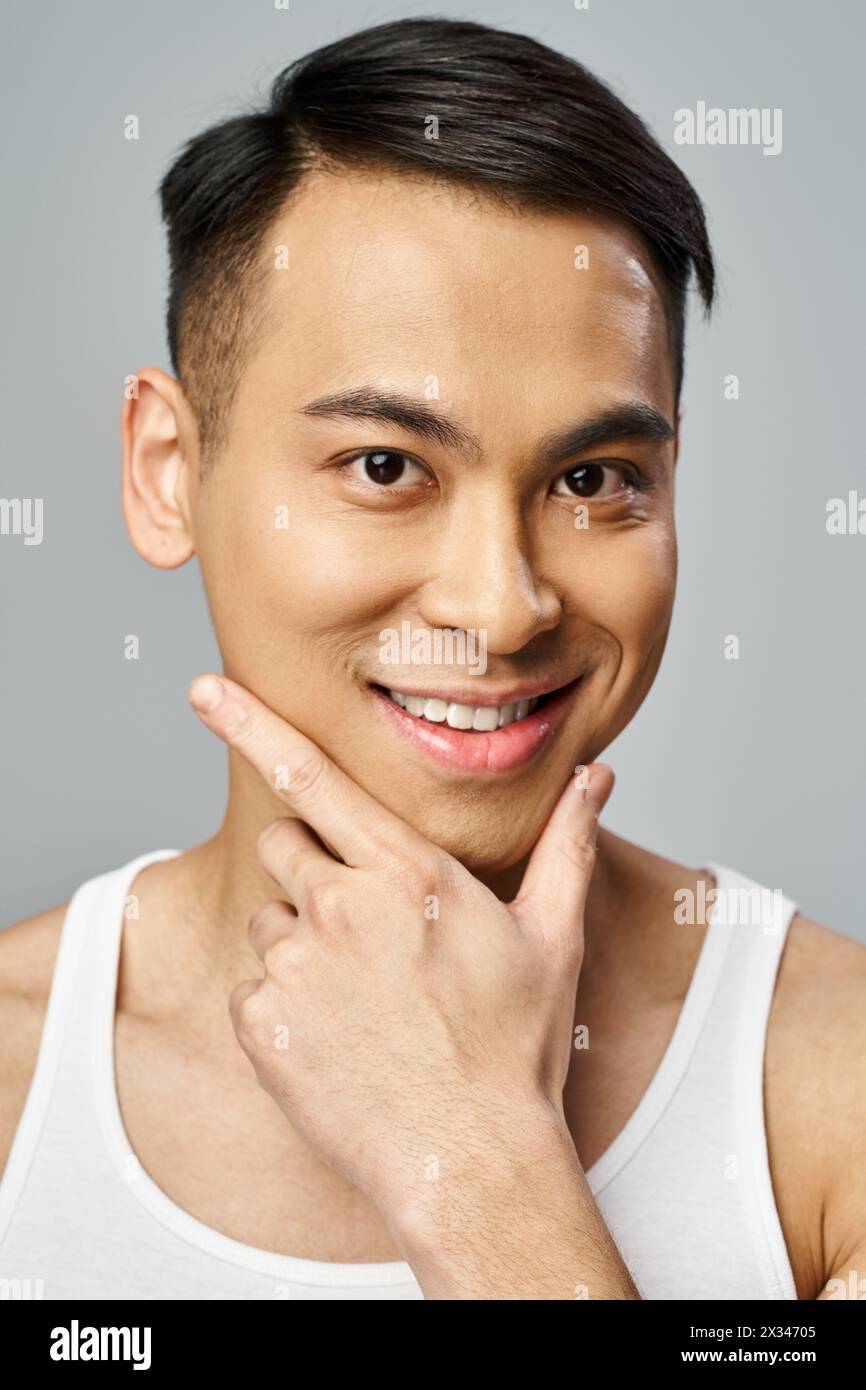 A handsome Asian man with a bright smile in a grey studio, exuding joy ...