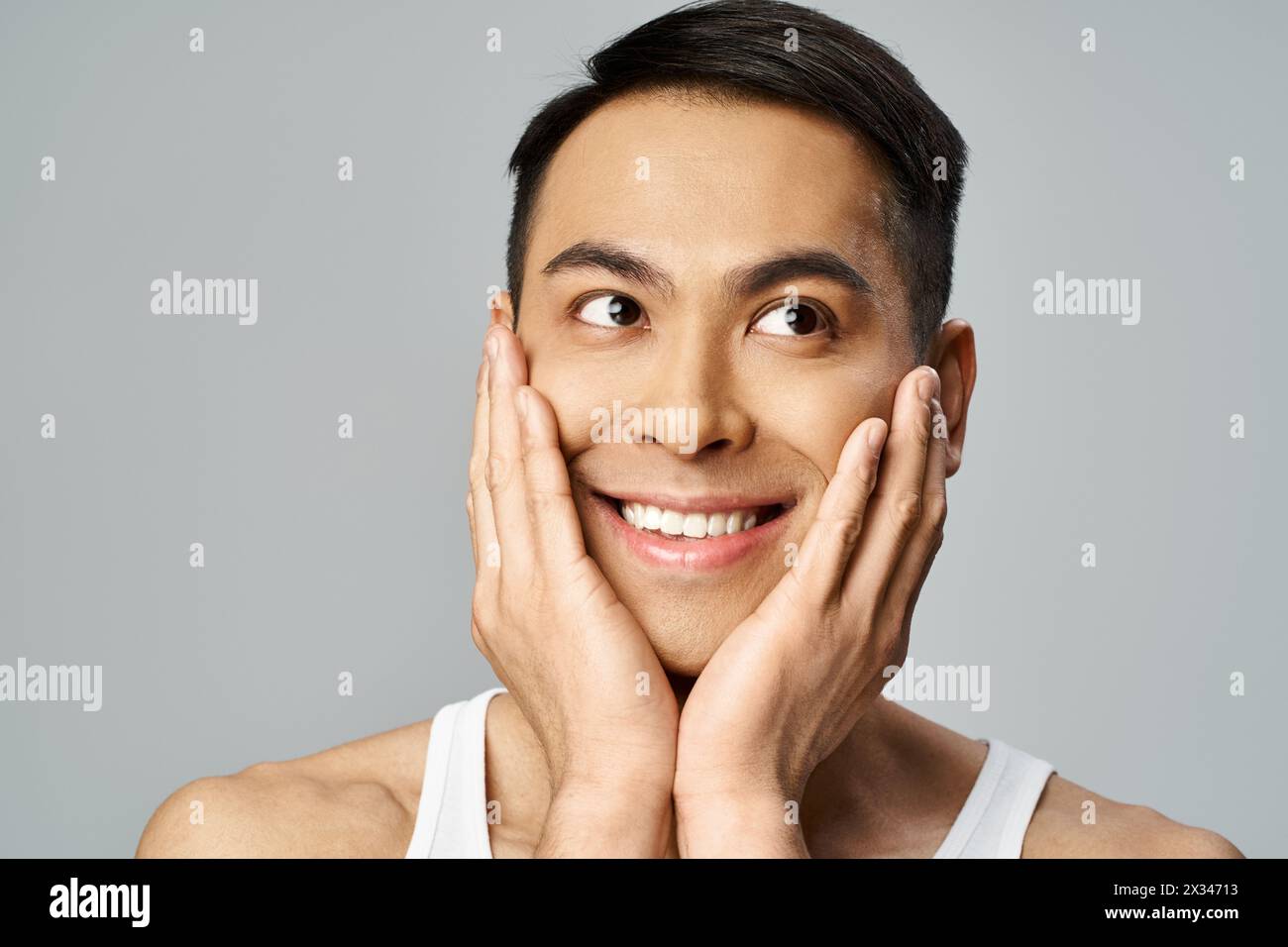 Handsome Asian man with a serene smile, gently touching his face in a ...