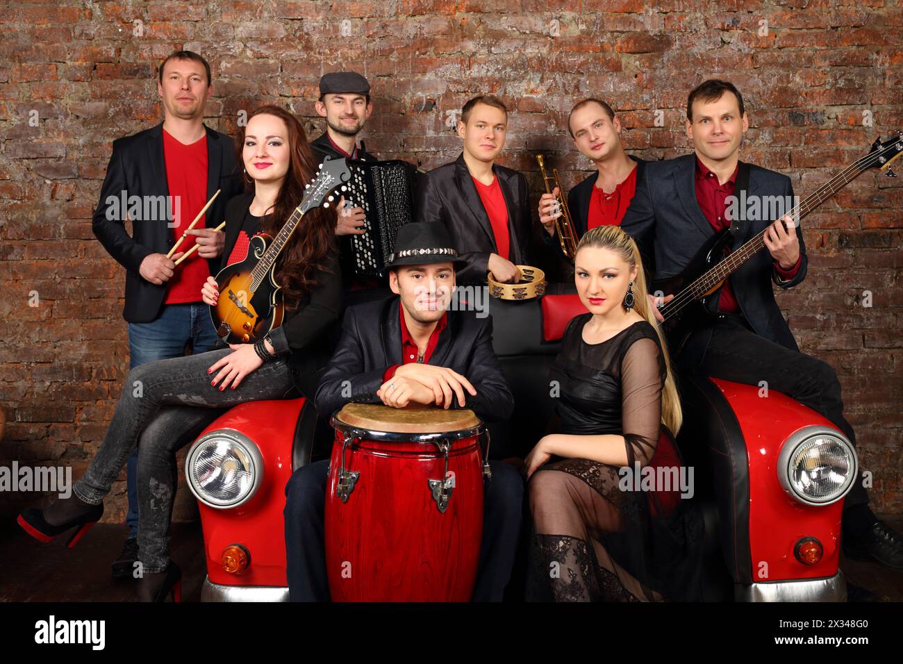 Brass band of eight people in red and black clothes pose in studio with ...