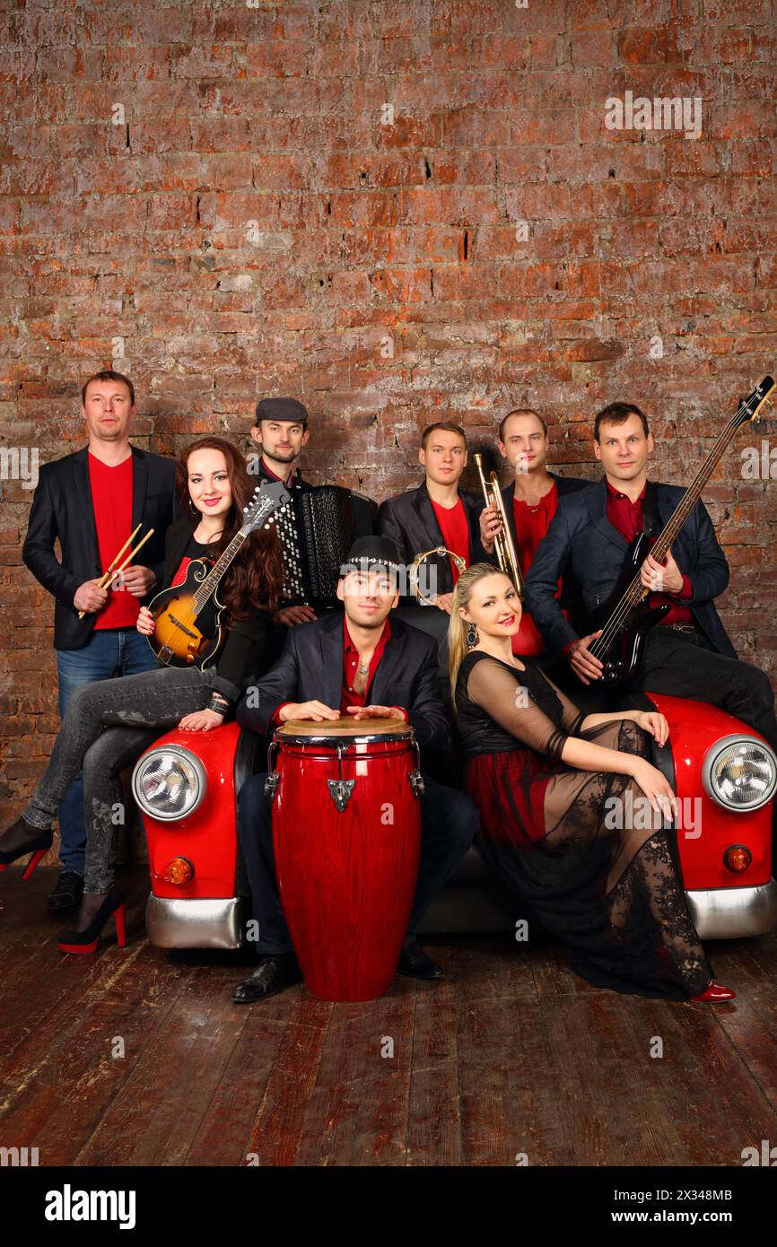 Brass band of eight people in red and black clothes pose in studio with ...
