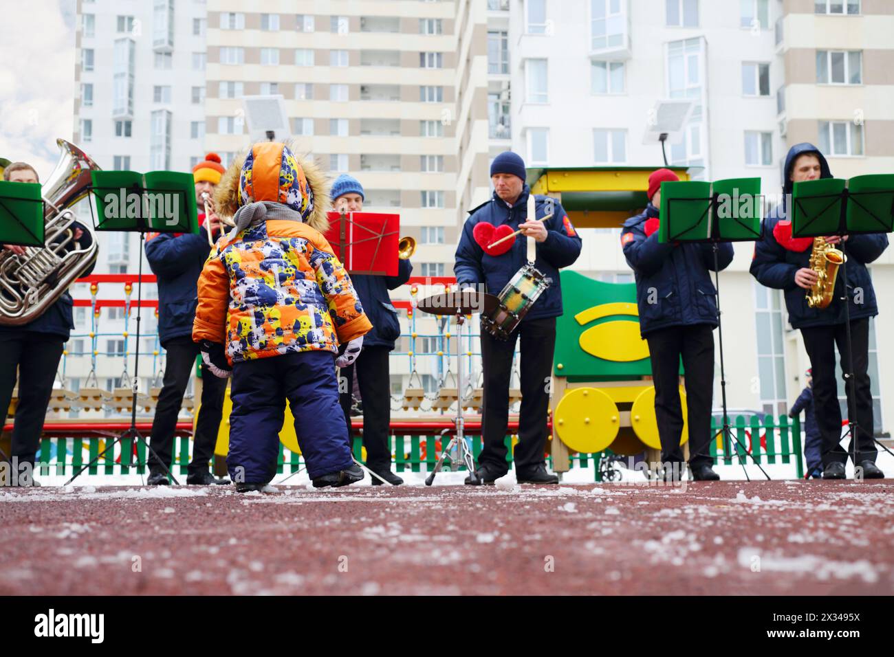 Brass band of six musicians play outdoor at winter day and kid listens ...