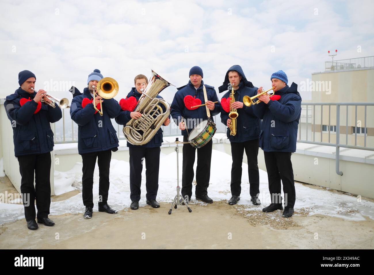 Brass band of six musicians play on roof of tall building at winter ...