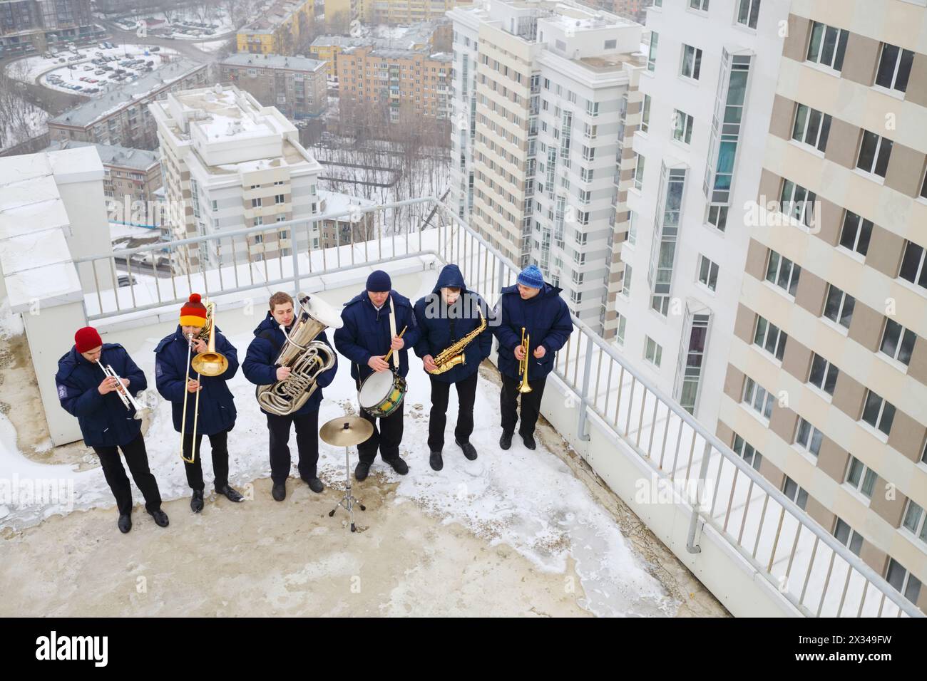 Brass band of six musicians play on roof of tall building at winter in ...