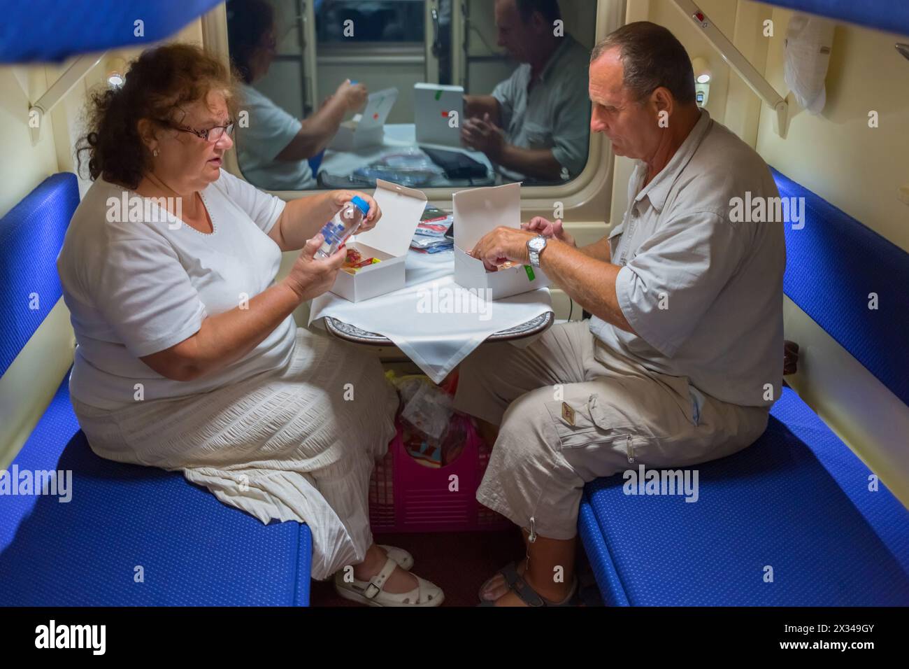 Man and woman eat, sitting in bench at table near window of moving ...