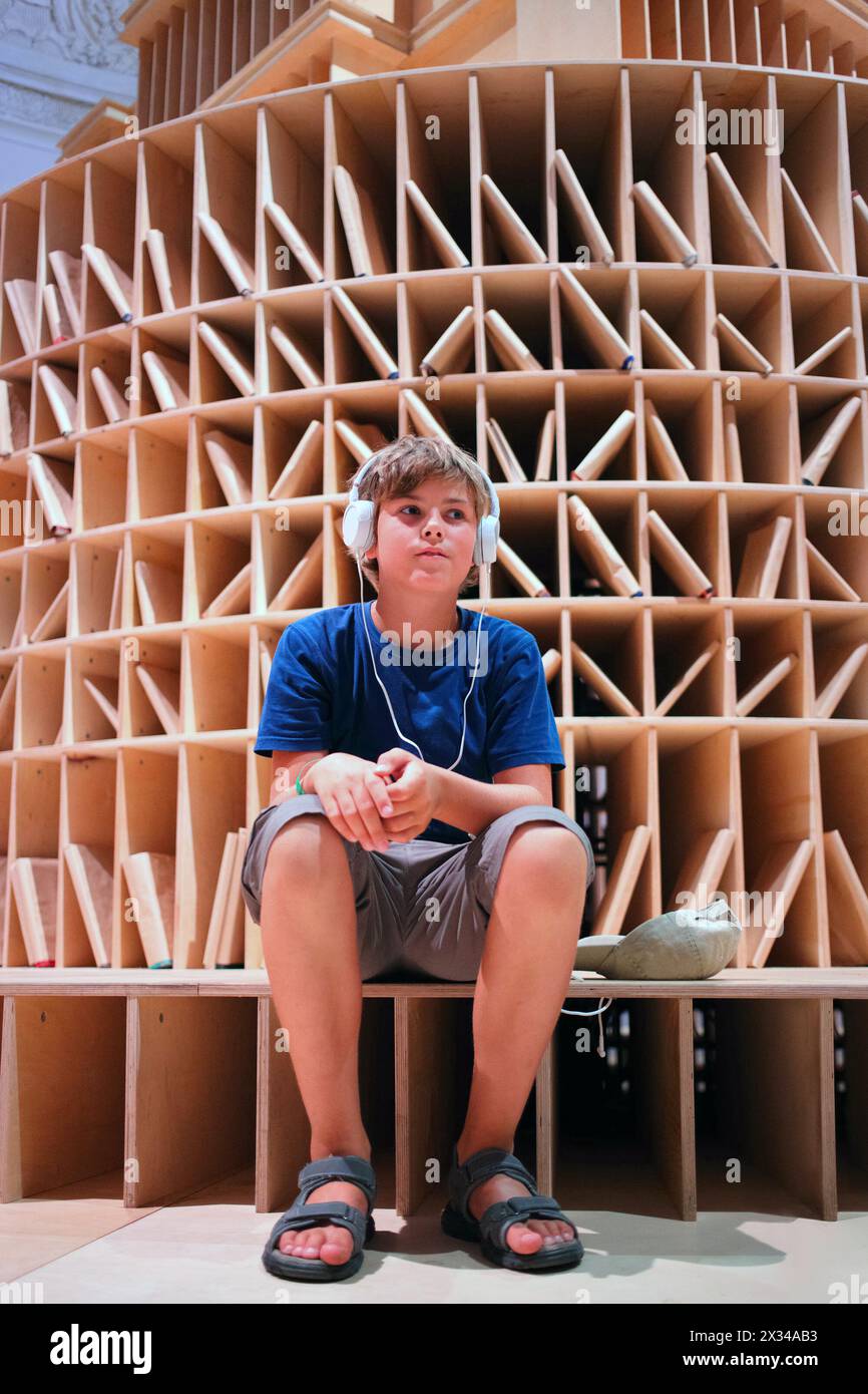 Boy sitting on bench near shelves of books in headphones Stock Photo ...
