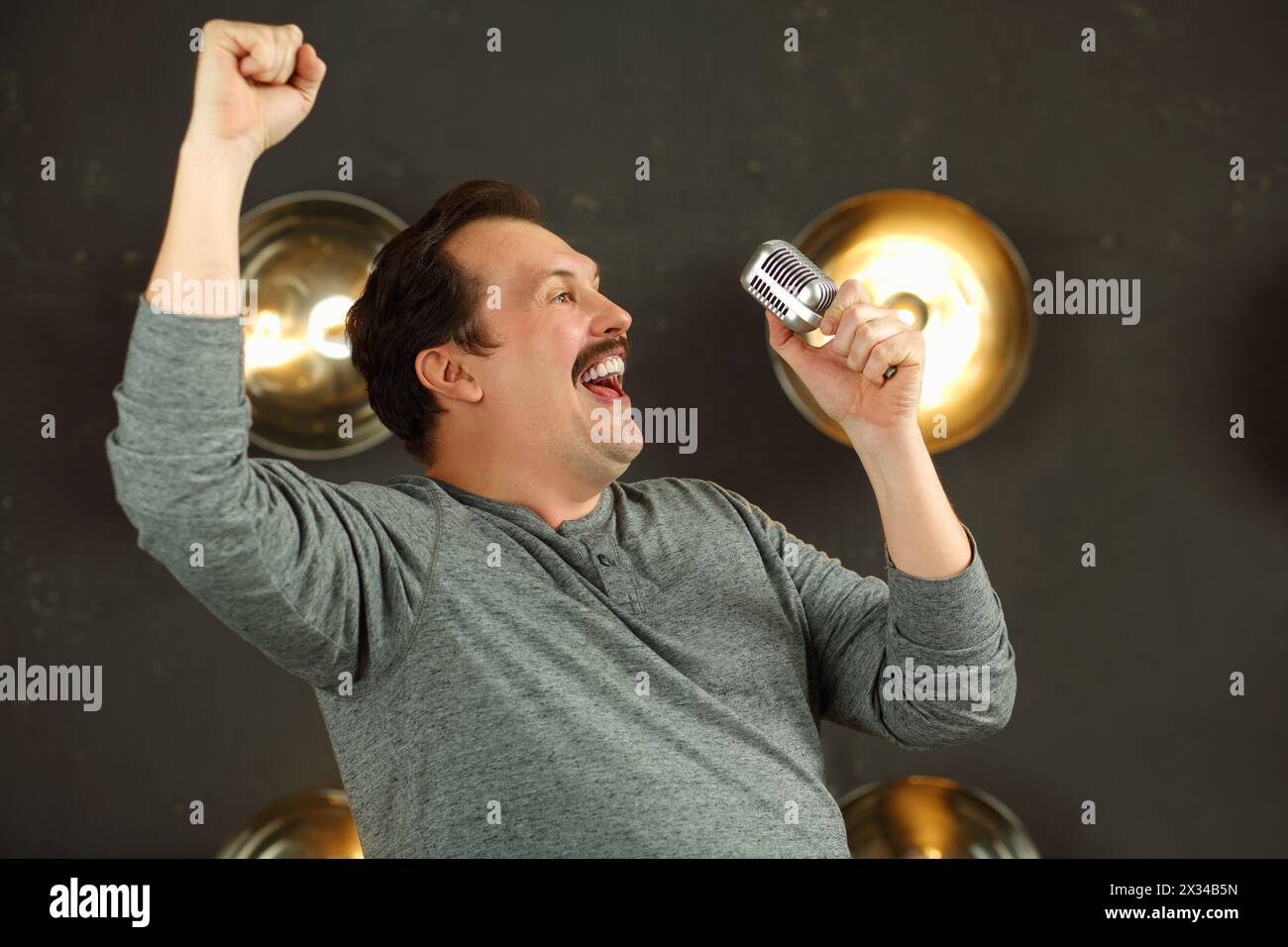 Smiling man with mustache sings with microphone in studio with lamps on ...