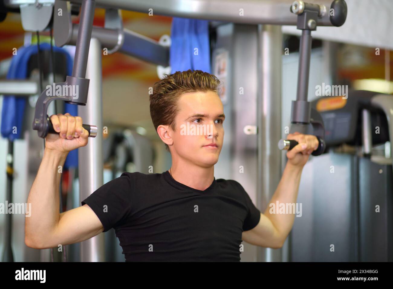 Young handsome man lowering weight of fitness machine in fitness club ...