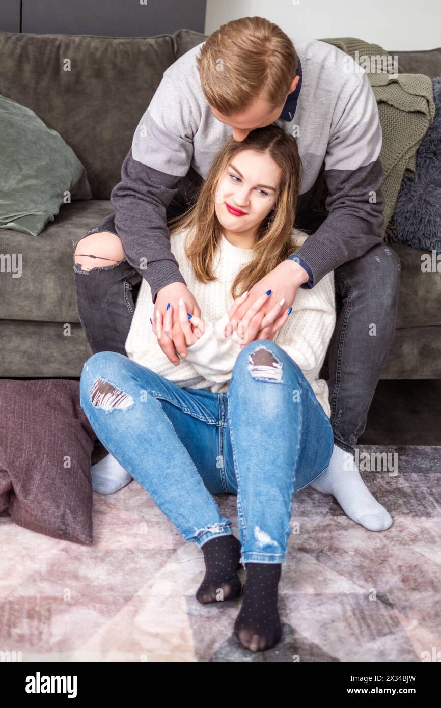 Playful home life scene, with a standing man hugging a seated woman ...