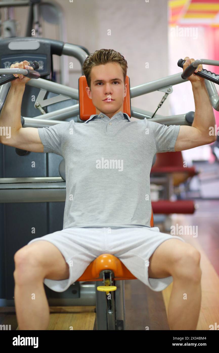 Young guy moving up and down his hands on fitness machine in fitness ...