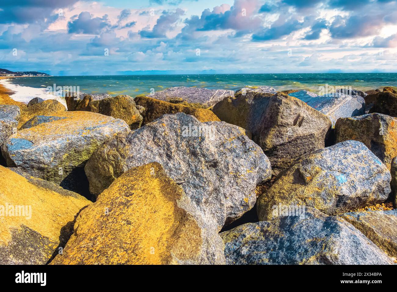 Large boulders as part of the sea defences with deep blue sky and calm ...