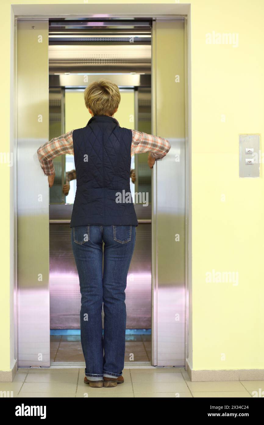 A woman in a vest and jeans pushing her hands the elevator doors, view ...