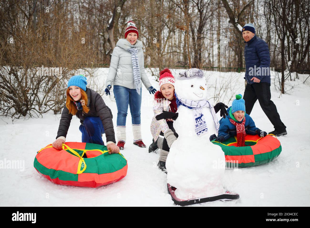 Three adults and two children play with snow tubes and snowman at ...
