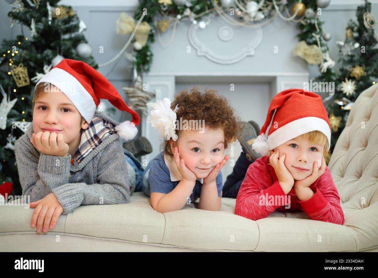 Three happy cute children in santa caps lie on couch and smile Stock ...
