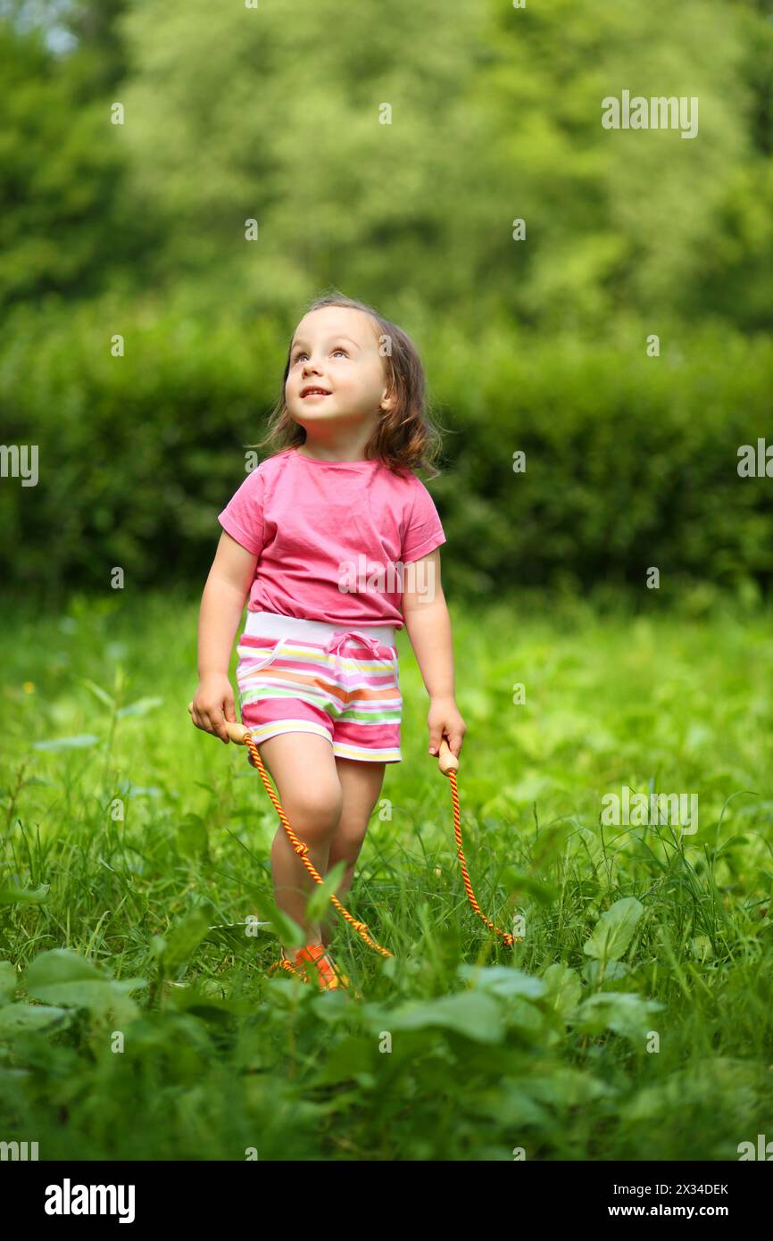 Little cute girl with skipping rope looks up in summer sunny garden ...