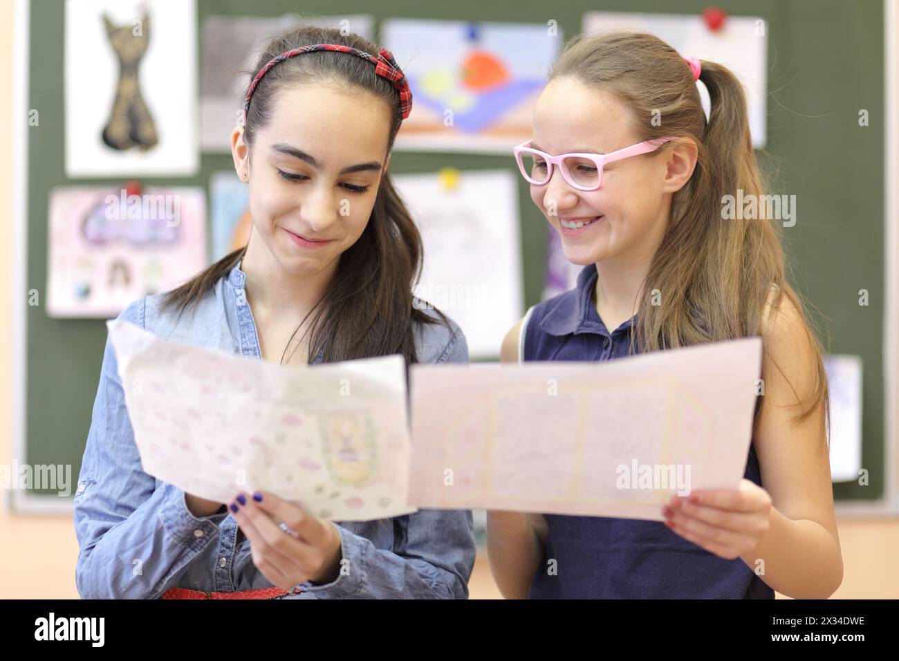 Two schoolgirls consider drawings on drawing lesson in classroom and ...
