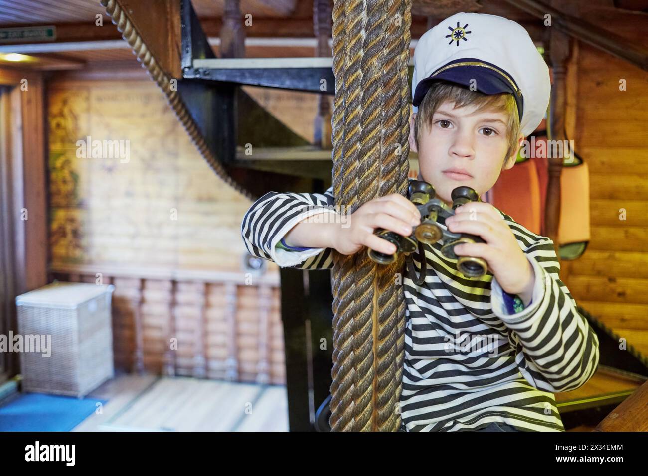Boy in striped vest and white cap with binoculars at room on pleasure ...