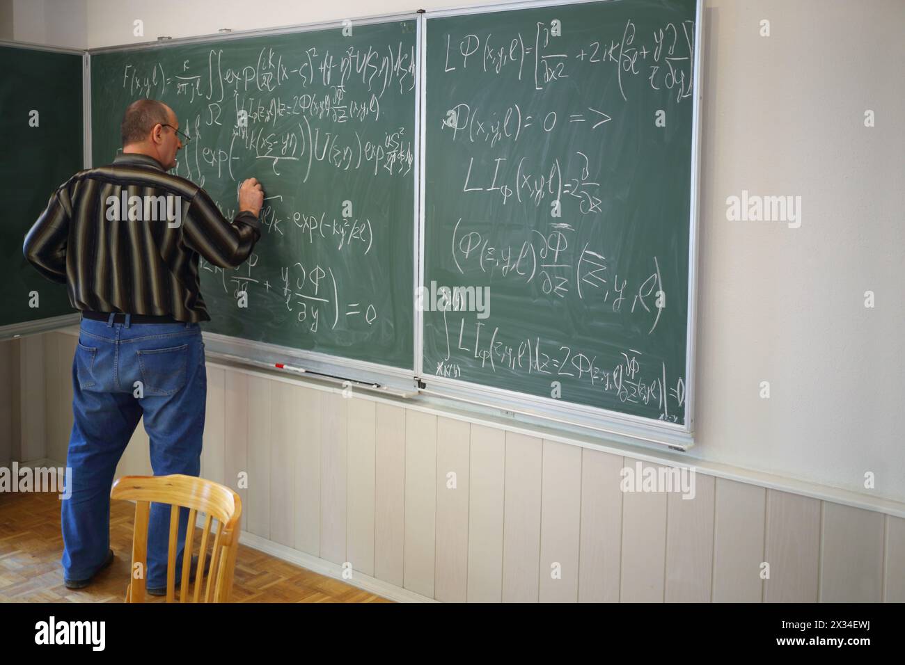 Teacher writes mathematics formulas on blackboard in school classroom ...
