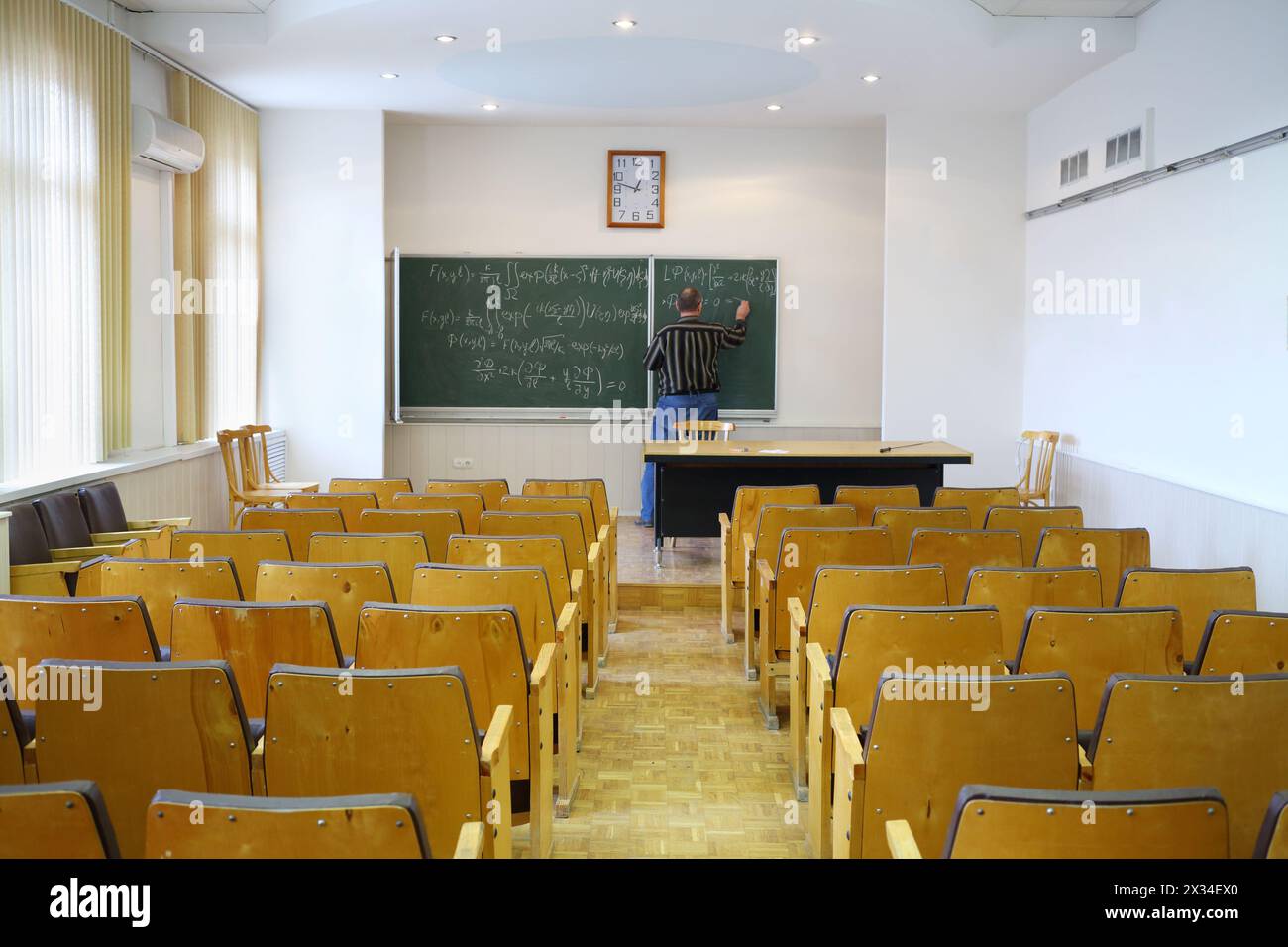 Teacher writes mathematics formulas on blackboard in school classroom ...