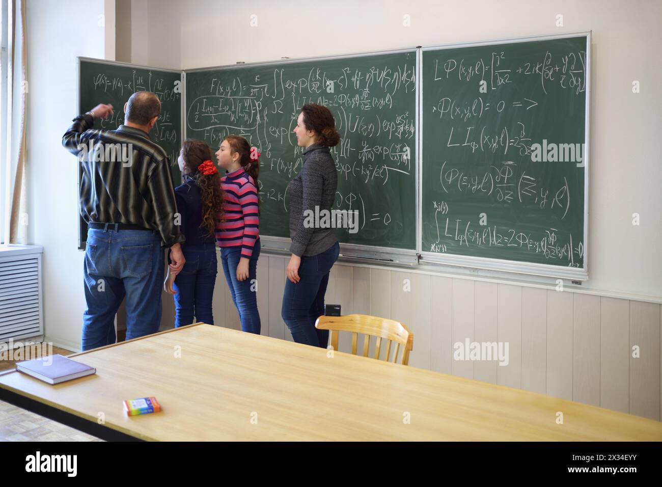 Two teachers and two girls stand near blackboard with formulas in ...