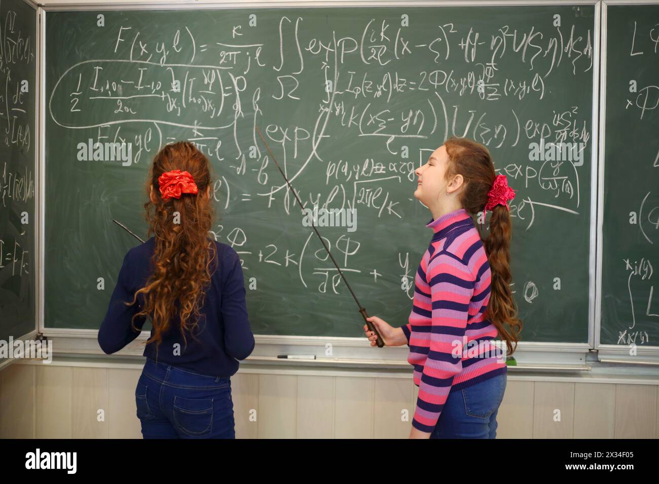 Two girls stand near blackboard with formulas in classroom and hold ...