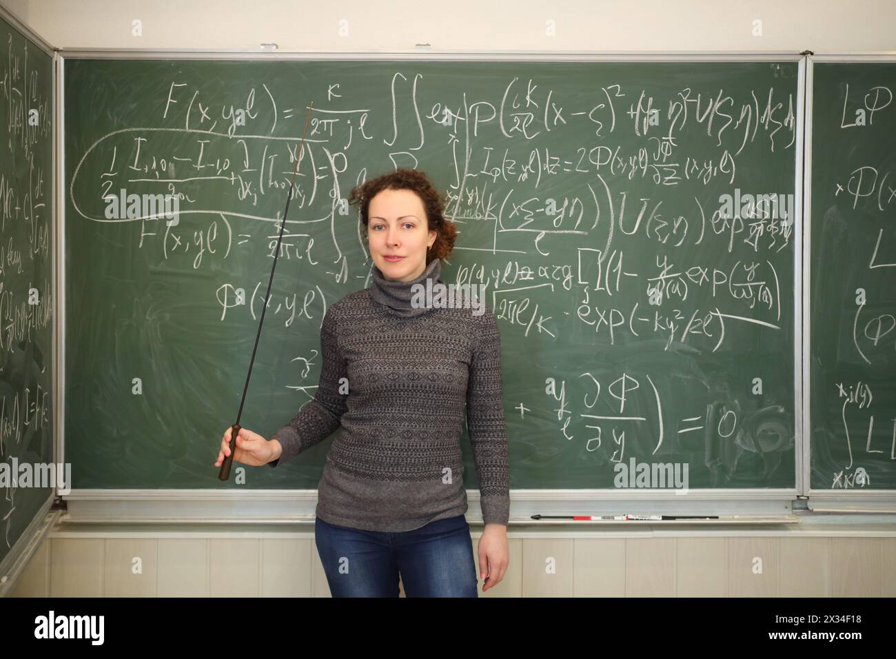 Teacher with pointer stands near blackboard with mathematics formulas ...