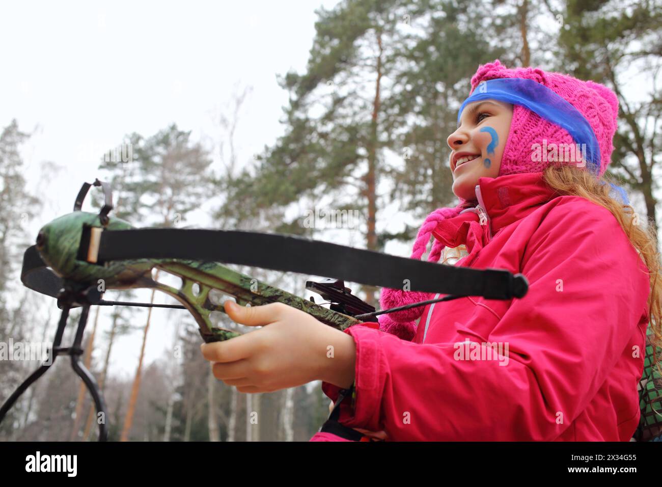 Girl with blue paint on his face and crossbow in her hands in forest ...