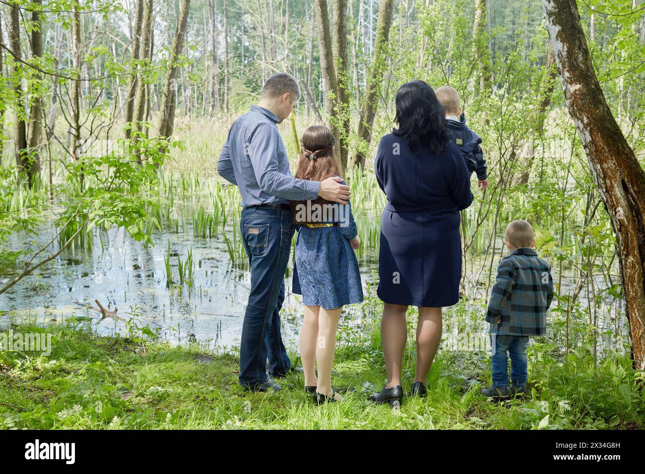 Family of five stands on boggy pond shore in summer park, rear view ...