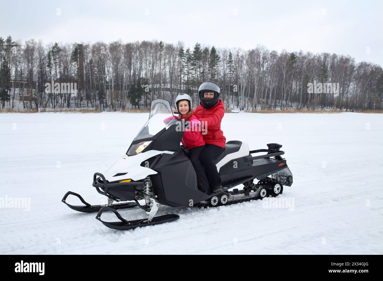 Mother with girl in helmets sitting behind the wheel of a snowmobile ...