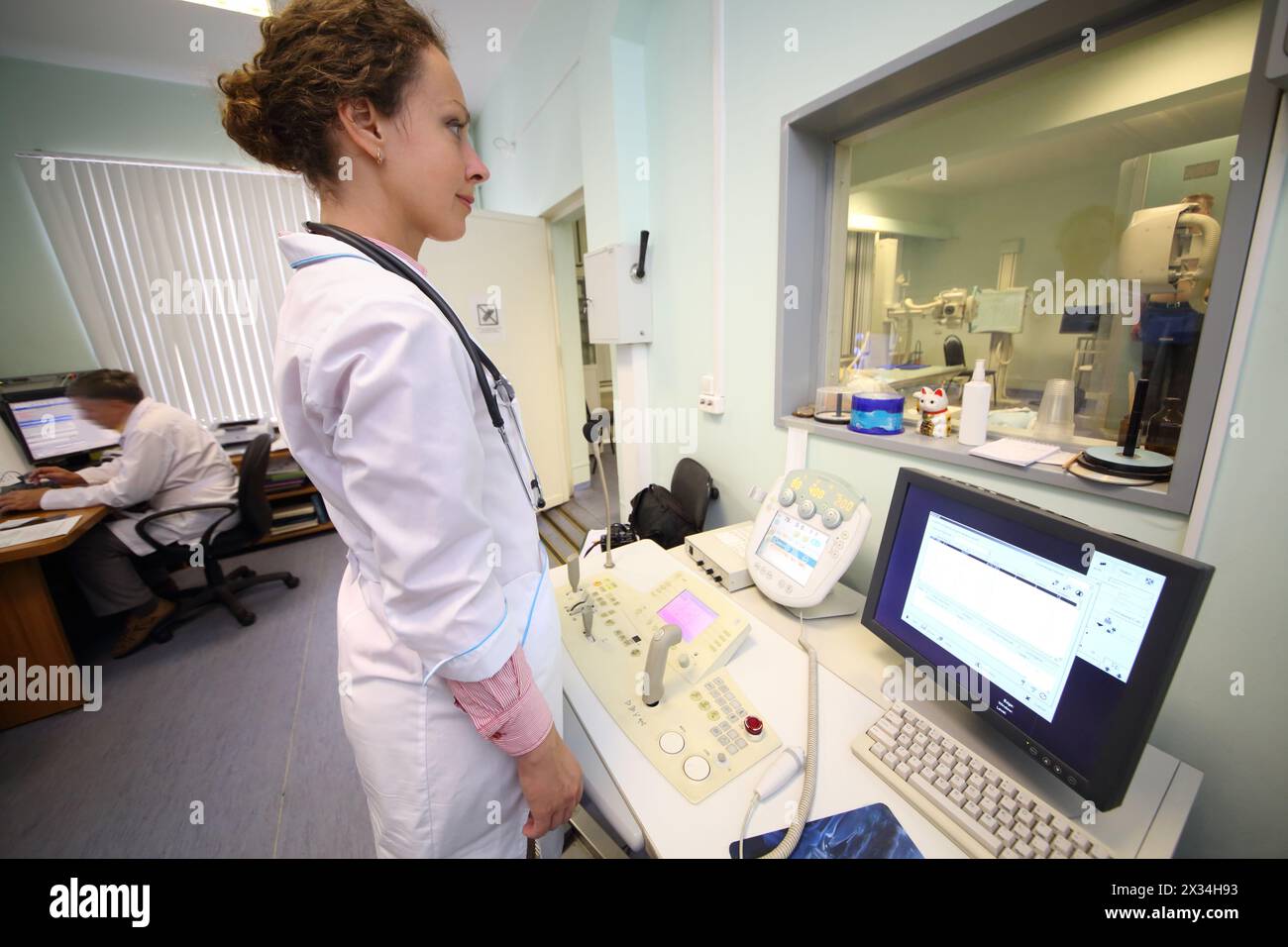 Doctor looks through a window in X-ray rooms at the control system ...