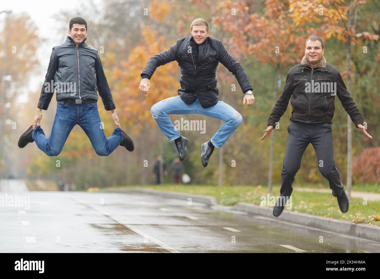 Three young men in black jackets jumping for fun in alley in park Stock ...