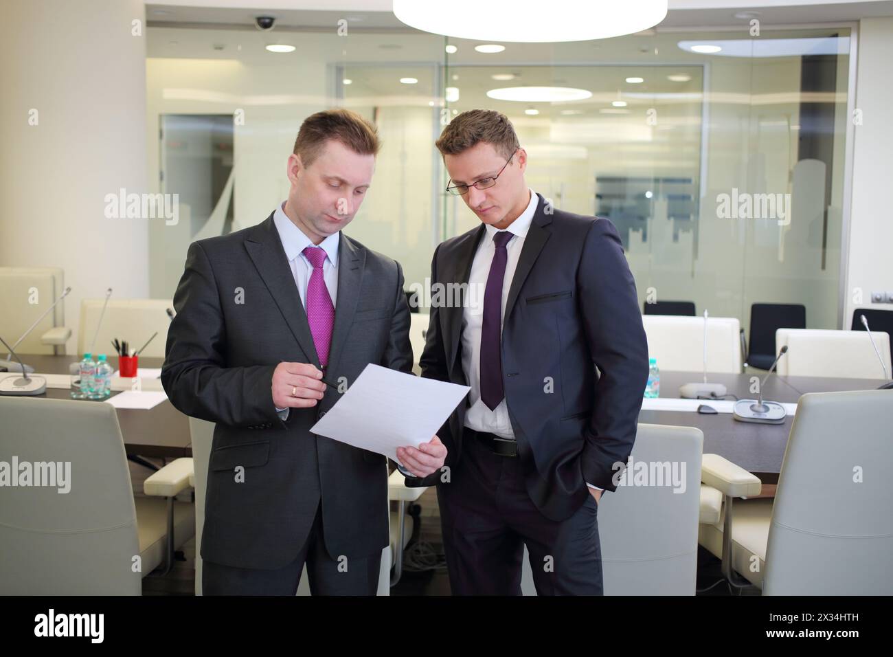 Two serious businessmen standing with a blank sheet of paper in ...