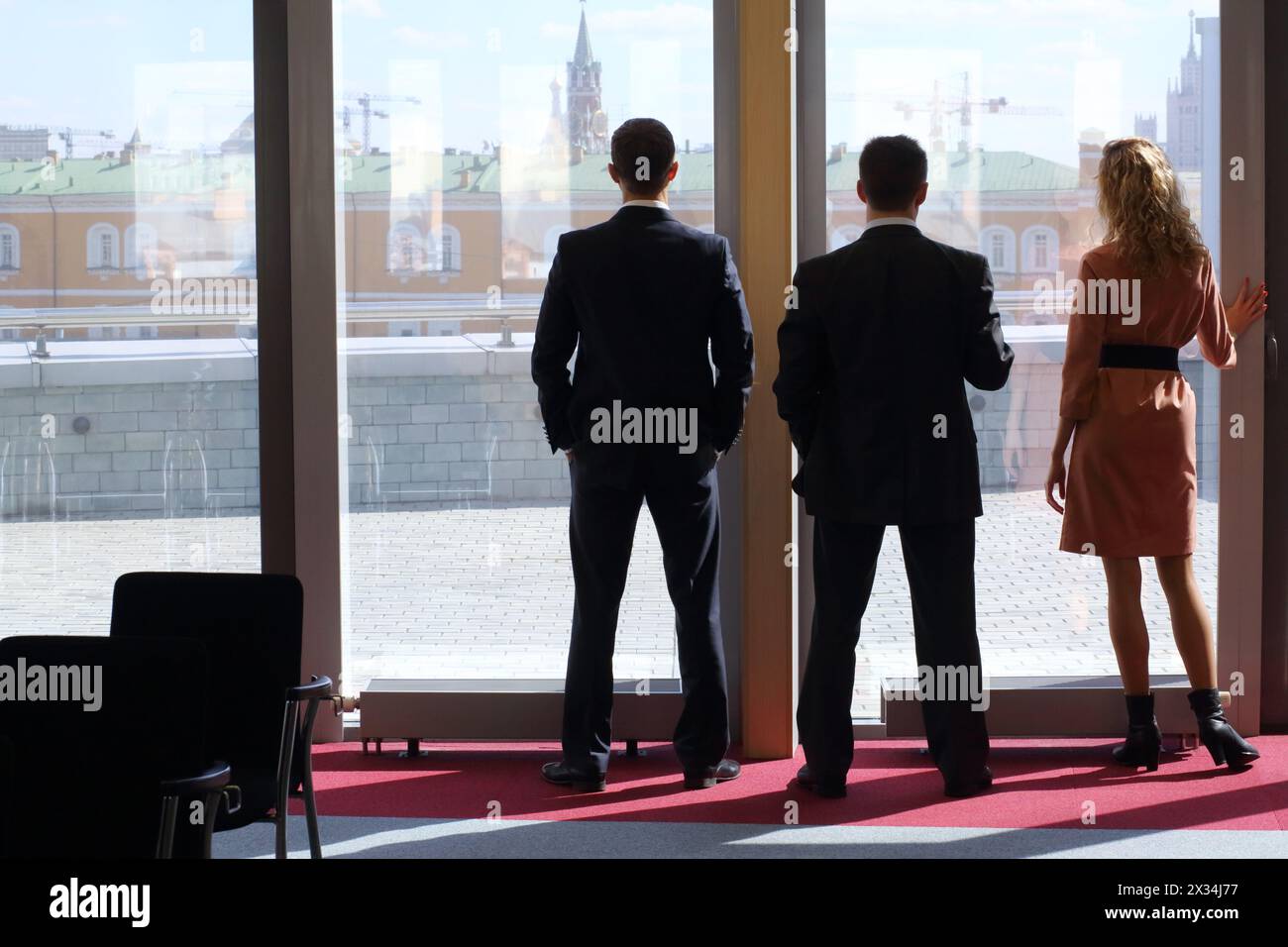 Group of businessmen: two men and a woman standing near big window with ...