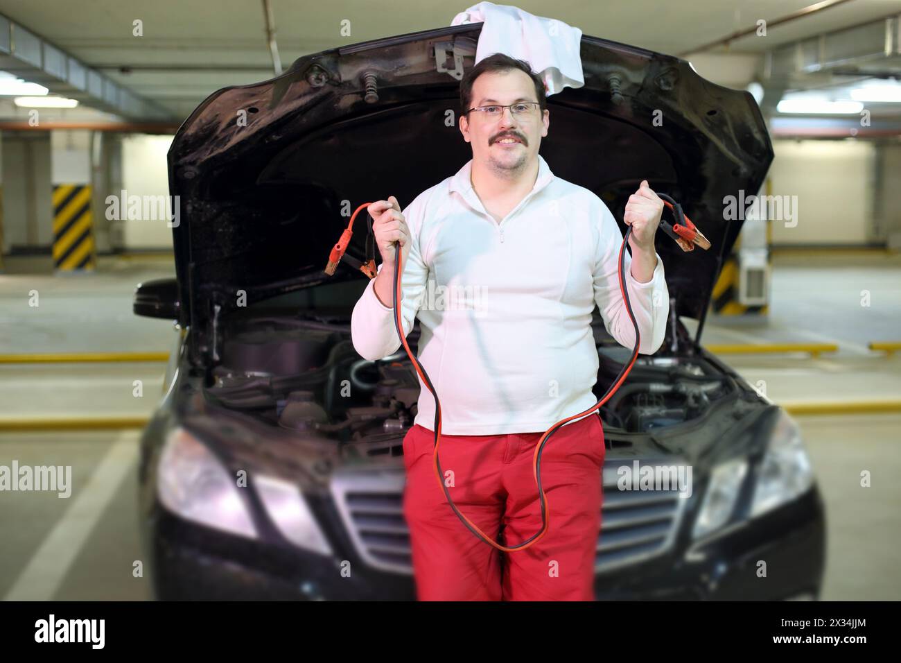Man with wires for recharging the battery near an open hood of the car ...